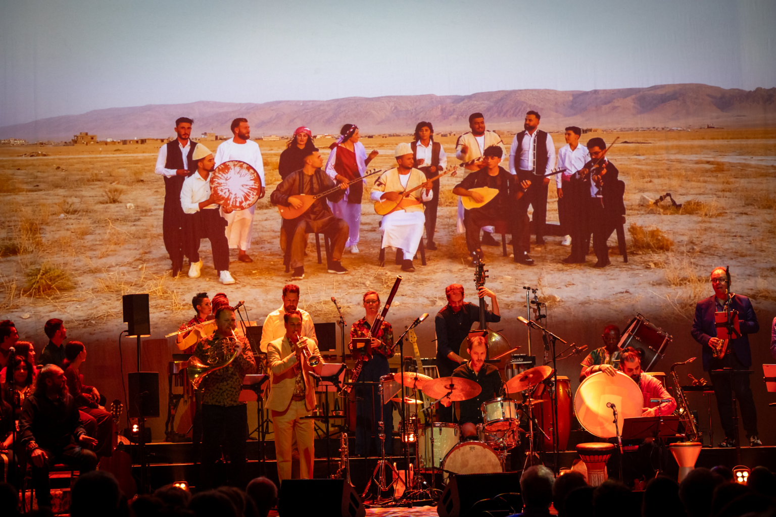 NBE speelt via een scherm met Irakese muzikanten op concert voor de Dag ...